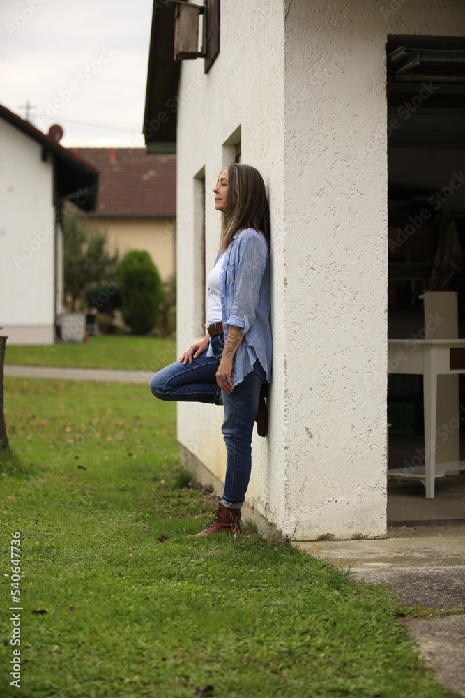 Eine Frau - Ü50 - im besten Alter lehnt an einer Hauswand und sieht in die Kamera. best Ager ...