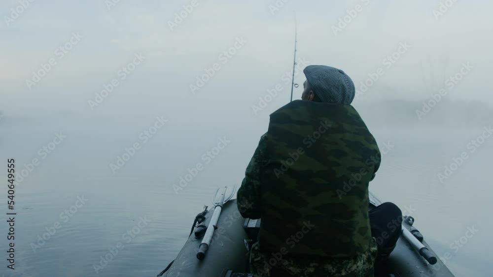 Back view of a male fisherman who is fishing from a boat. Morning ...