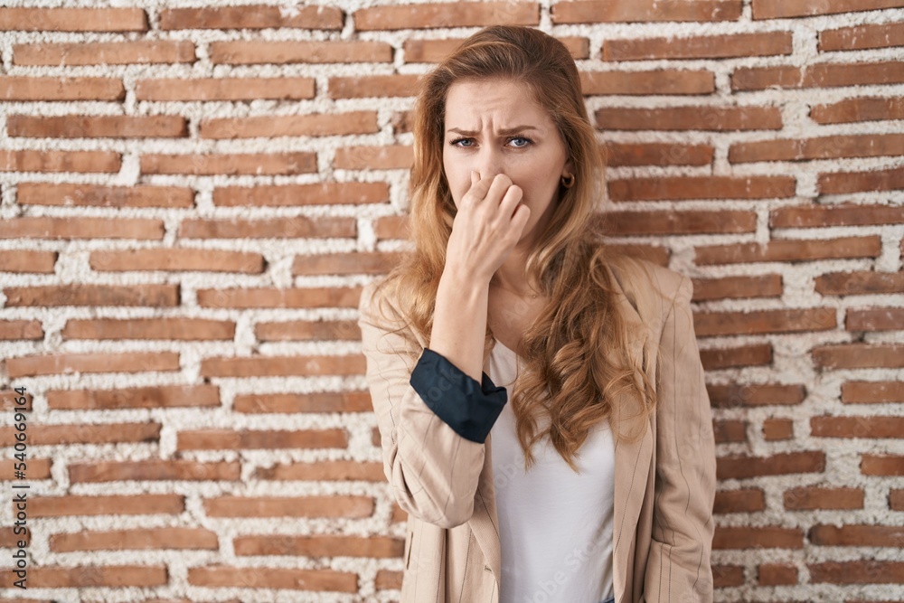 Beautiful blonde woman standing over bricks wall smelling something ...