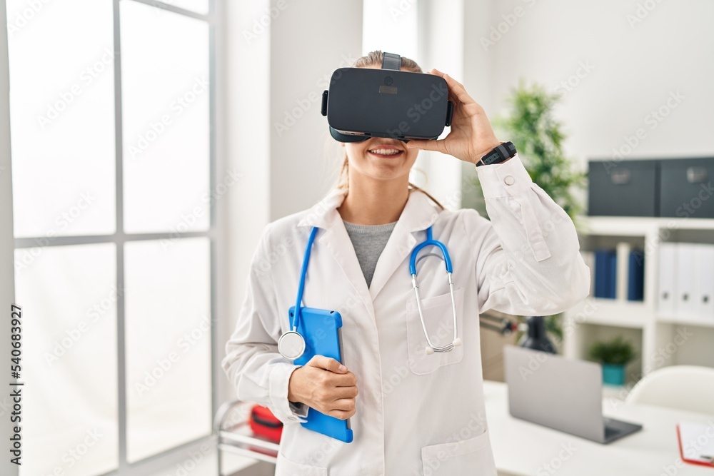 Young blonde woman wearing doctor uniform using touchpad and vr goggles ...