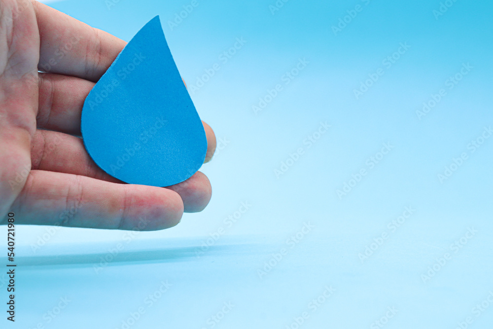 Hands holding a paper water drop on a blue background. Concept save ...