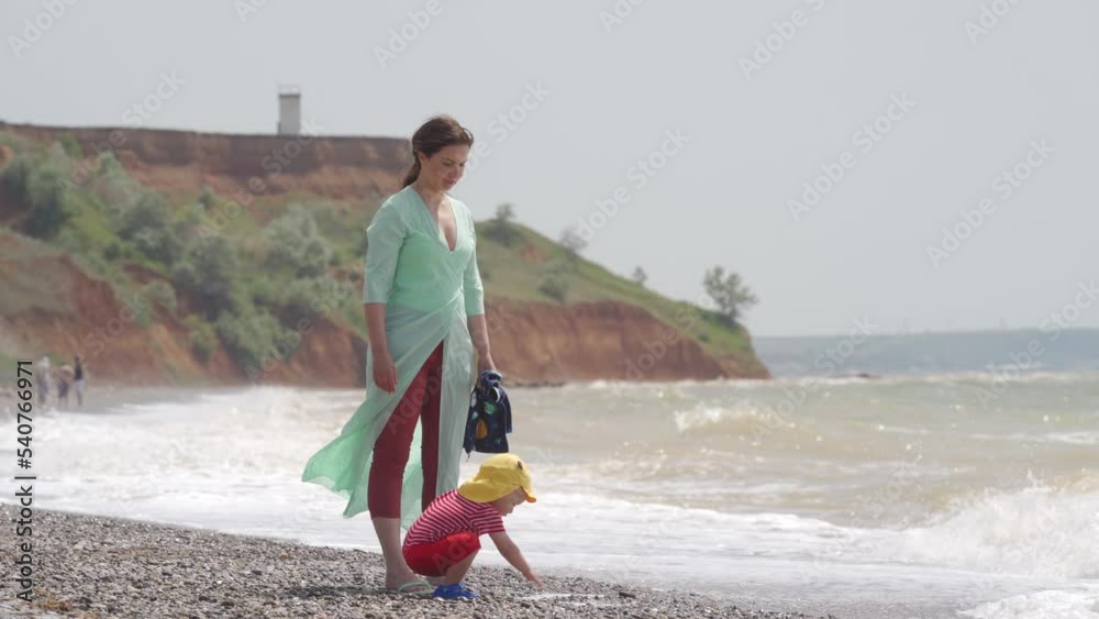 Mother and little cute child are walking on a windy beach along the ...