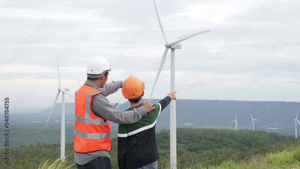Engineer with his son on a wind farm atop a hill or mountain in the ...