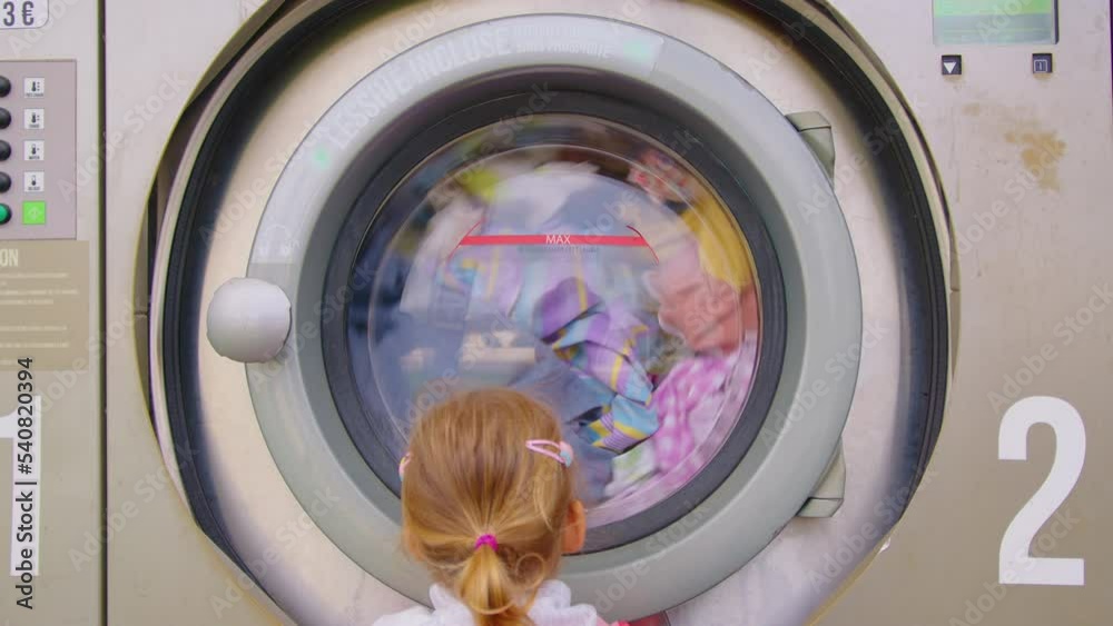 Little girl regular housekeeping work out towels into washing machine ...