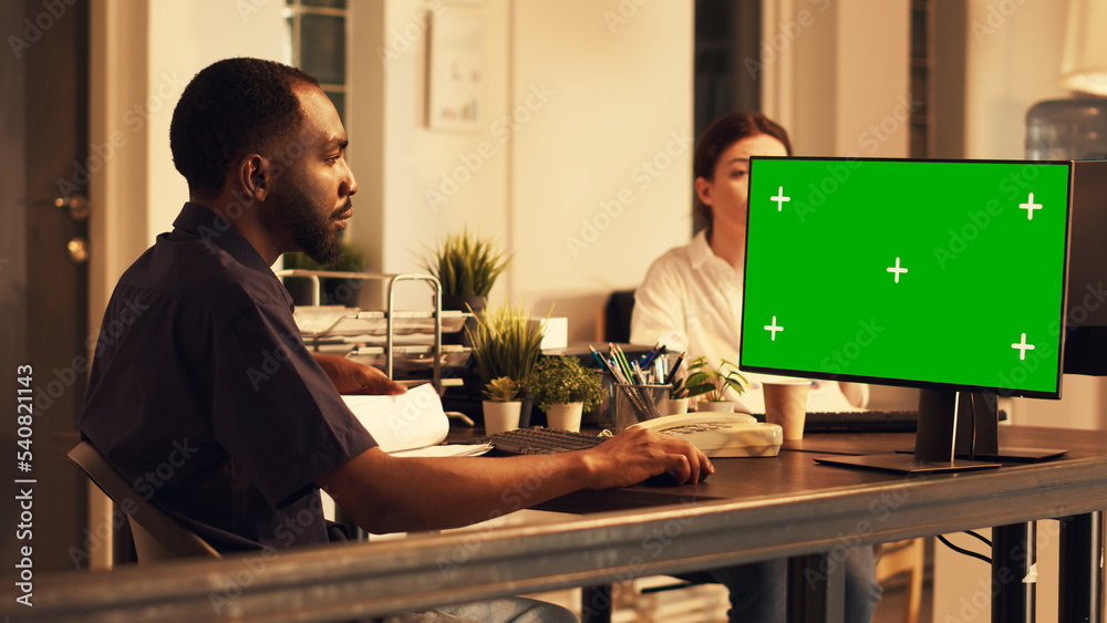 Male manager looking at computer with greenscreen display, working with ...