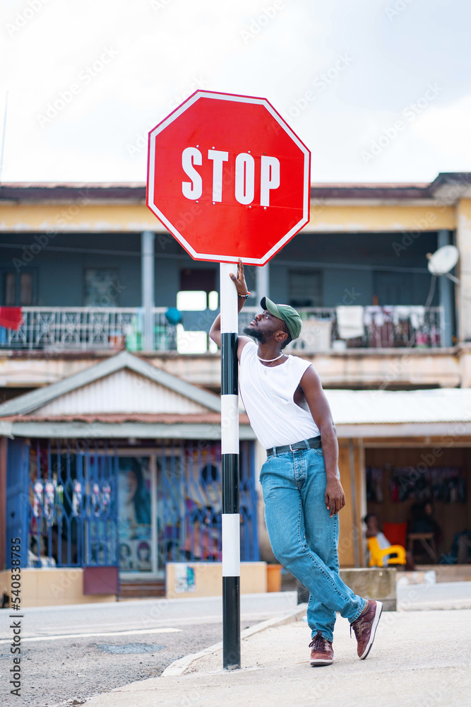 image of metal erected pole with a stop sign, african guy leaning ...