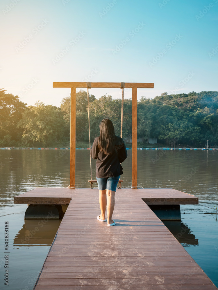 Back view of young Asian woman walking to play a wooden bench swings in ...