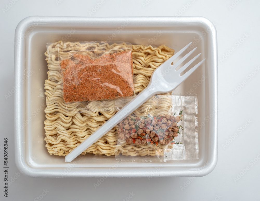 Dried block of instant noodle with seasoning sachets and plastic fork ...