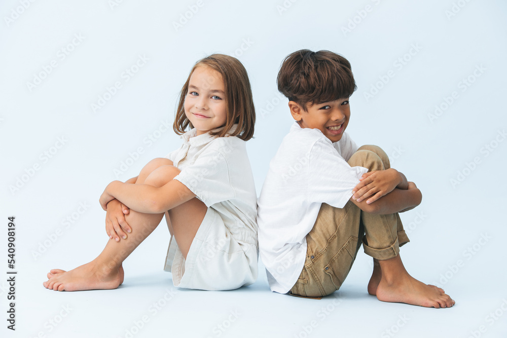 Fun portrait of awkwardly smiling boy and girl sitting back to back on ...