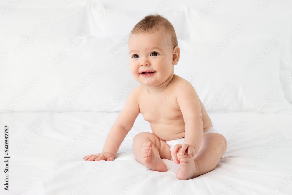 Cute baby sitting on white bed holding foot Stock Photo | Adobe Stock