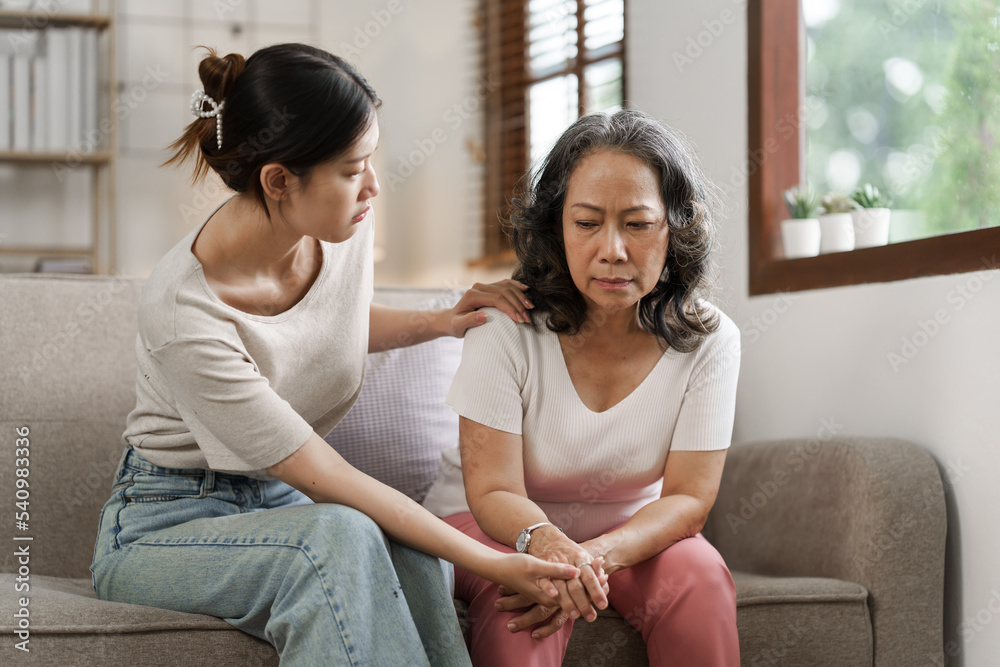 Sad asian mature woman grown up daughter or grandkid sitting on sofa ...
