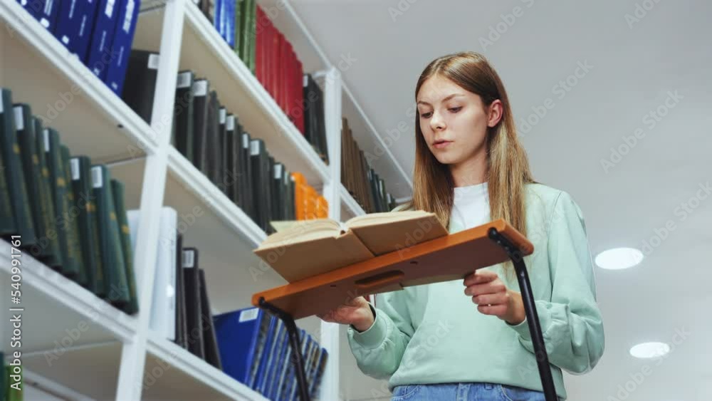 Caucasian teenage girl standing on ladder in library and reading book ... Caucasian teenage girl standing on ladder in library and reading book ...