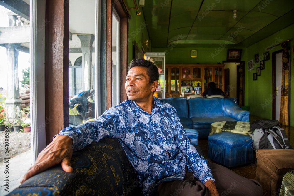 A local Indonesian man sits on the couch in his home in the small town ...