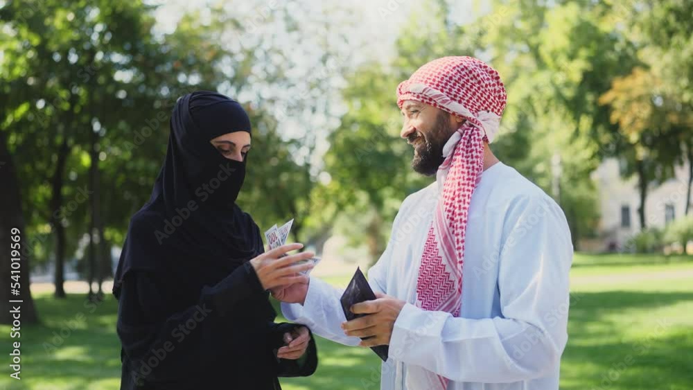 Arab man in white dress giving money to his wife in burqa, muslim ...