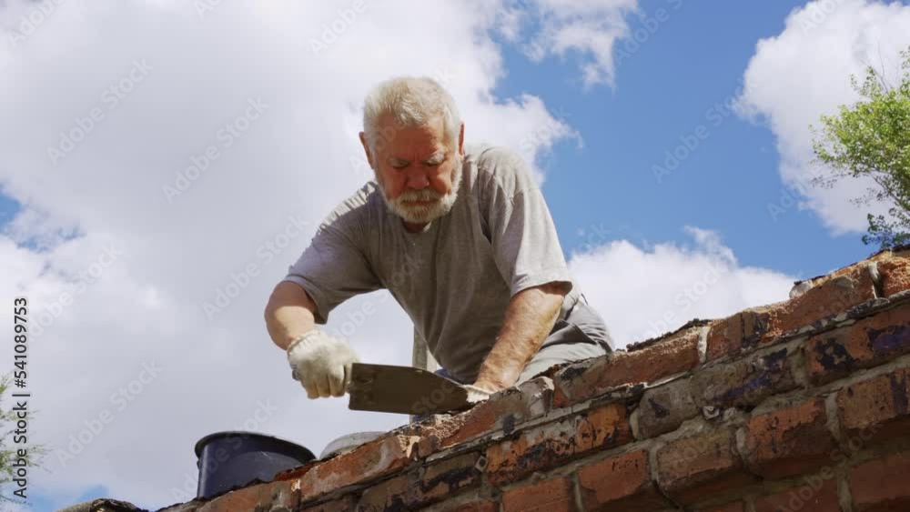 an elderly man dismantles the old brickwork and lays new bricks on the ...