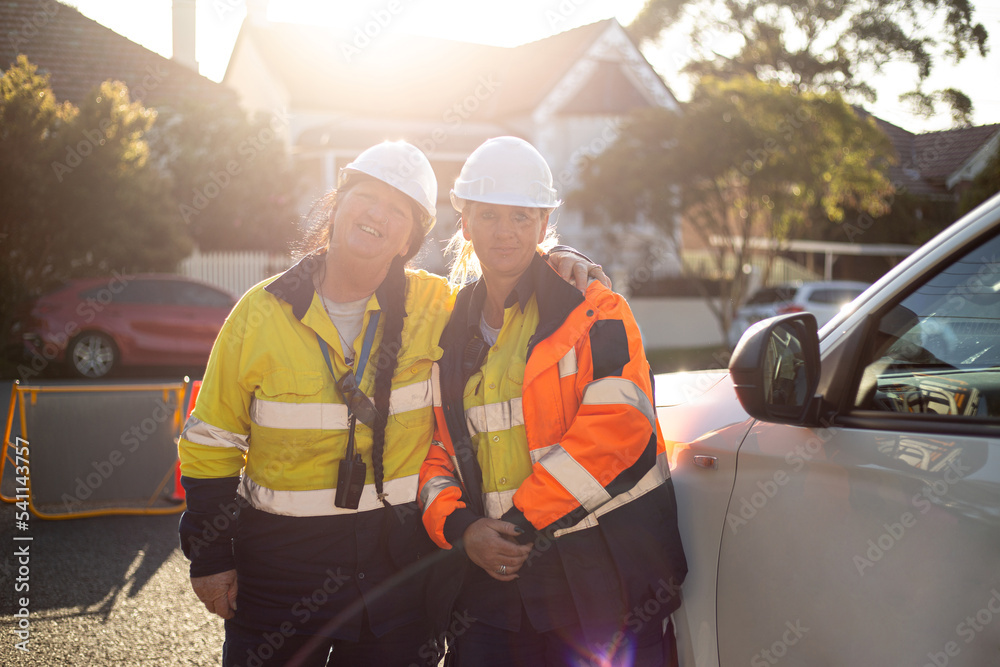 Two smiling women road workers wearing white helmet with orange and ...