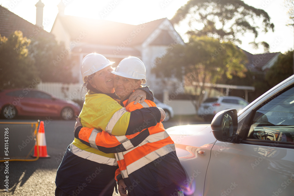 Two smiling women road workers with white helmets hugging each other ...