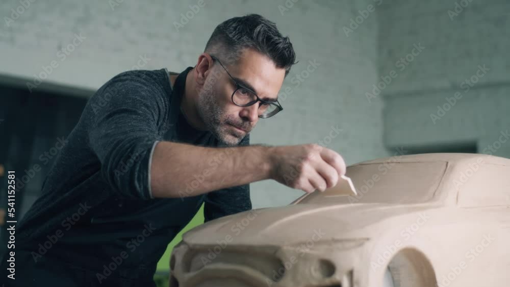 Experienced automotive designer with an apron works on the clay ...