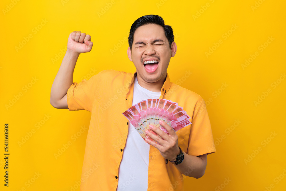 Excited young handsome Asian man holding bunch of money and celebrating ...