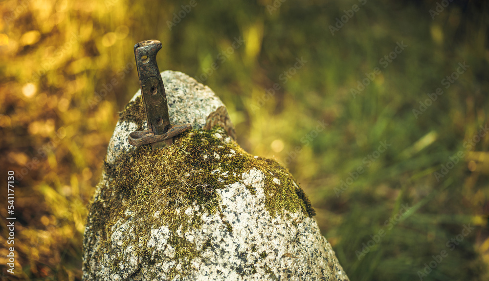 The handle of an old sword sticks out of a granite stone. A sword stuck ...