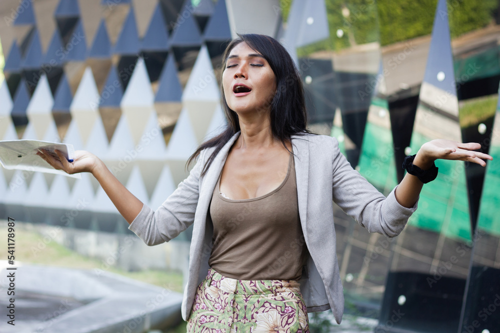 Sexy Thai woman with open arms holding documents folder with relief expression outside glass ...