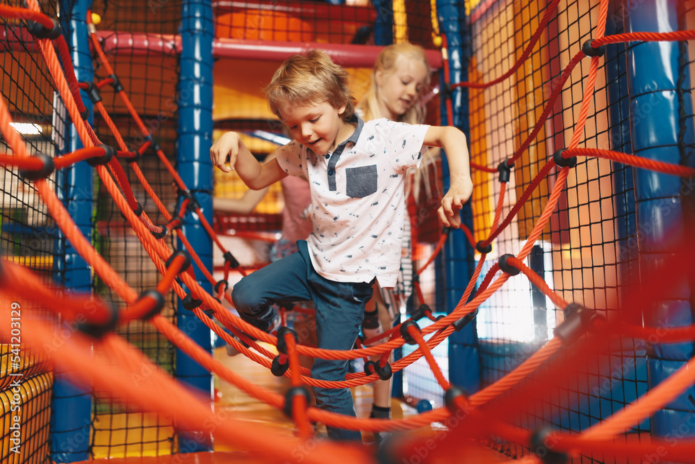 Excited kids playing together on net ropes. Happy group of siblings ...