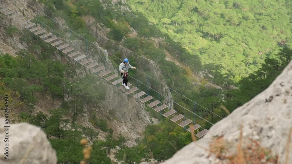 Woman tourist walking on suspension bridge in mountains over abyss ...