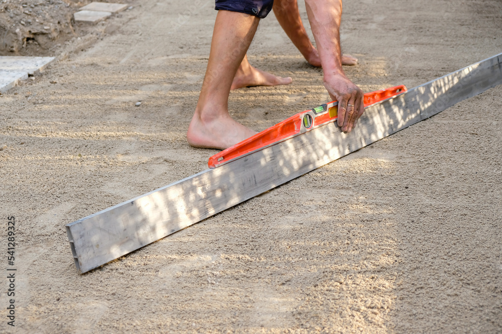 A spirit level in man's hands. A barefoot man levels the sandy platform ...