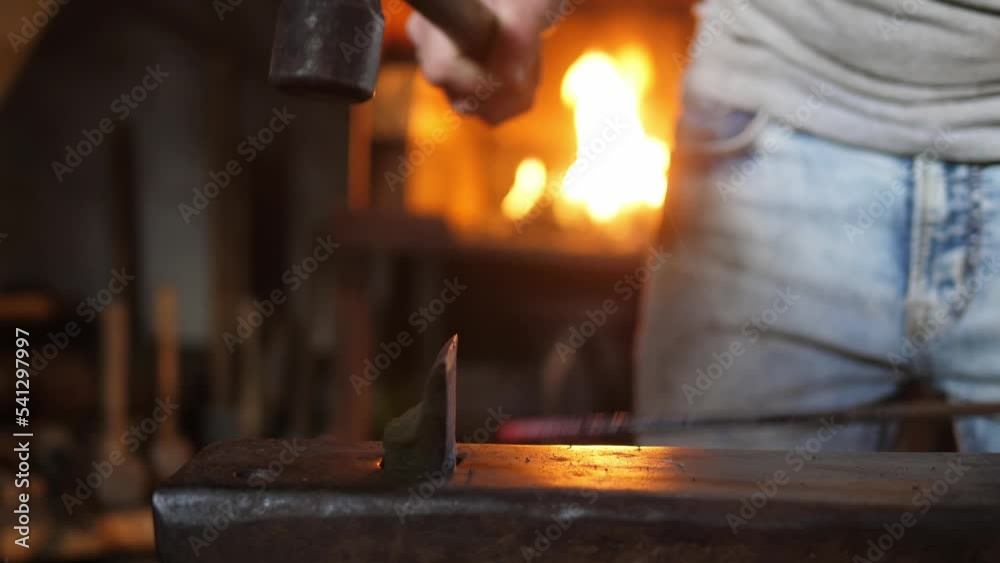 Blacksmith striking and breaking red hot metal rod with hammer on anvil ...