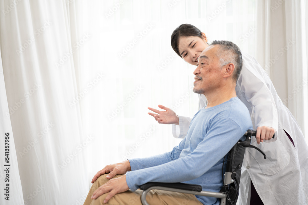 Impaired senior man in wheelchair and young asian female doctor taking ...