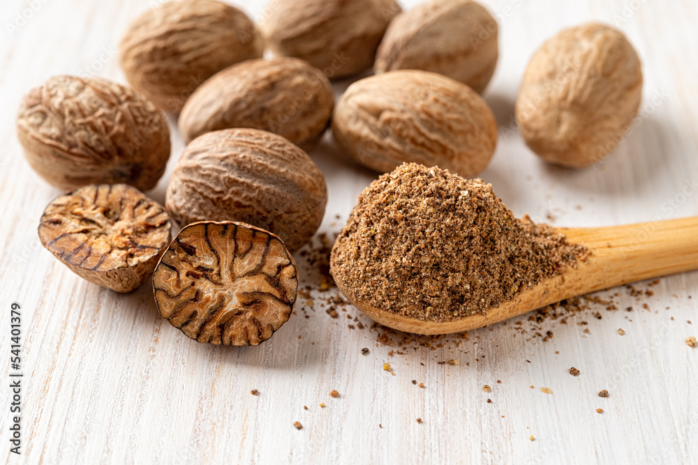 Spoon of ground nutmeg, whole and halved seeds over white wooden ...