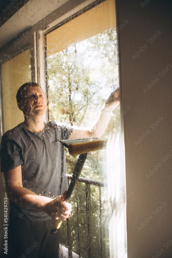 The man washes the windows at home using a window mop, cleaning the ...
