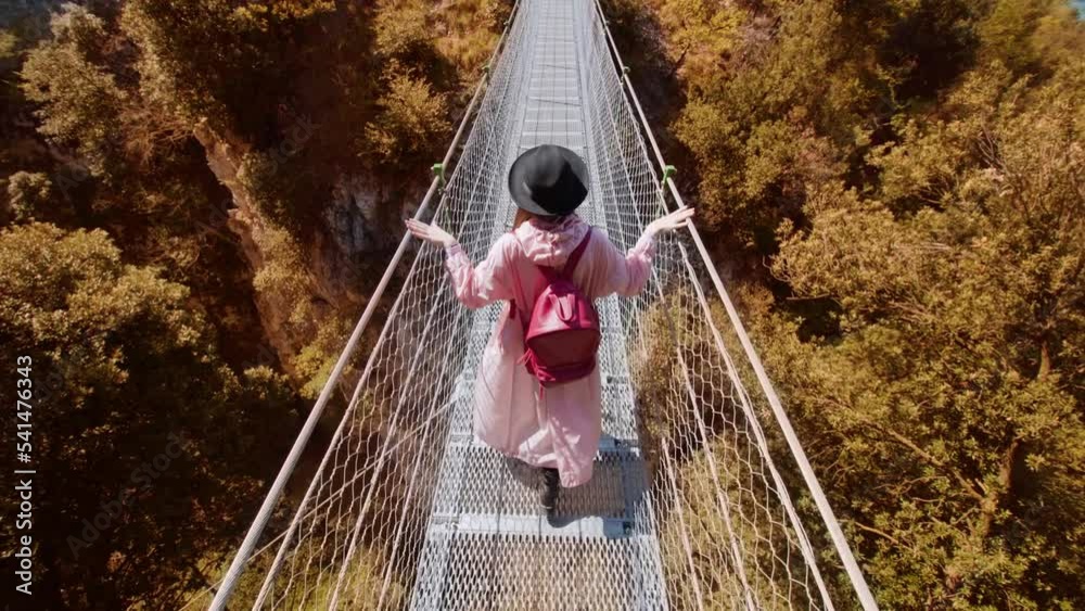 Woman in hat walks on footbridge over gorge among lush yellowed trees ...