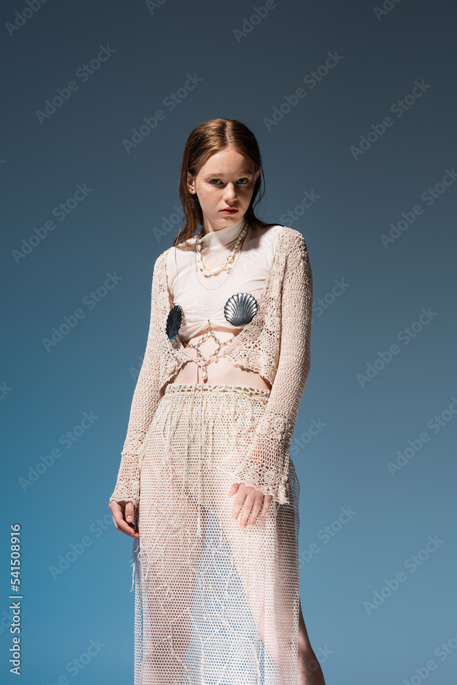 Stylish young model in fishnet skirt and cardigan looking at camera on ...