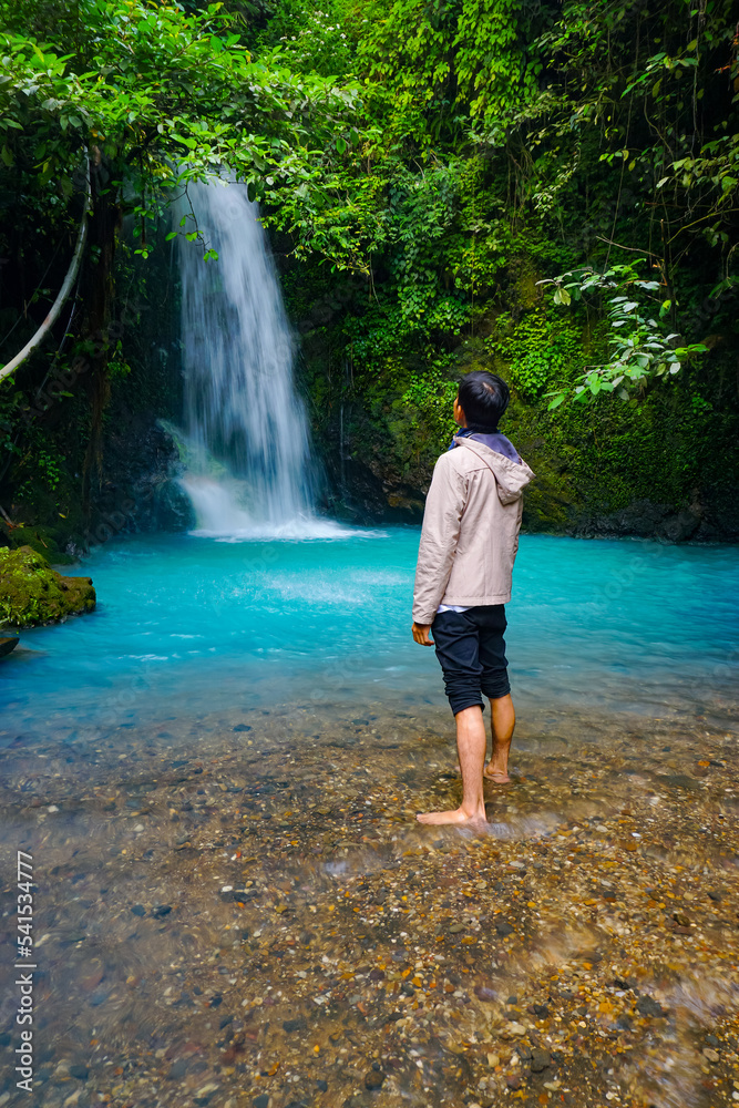 Young man standing on the front of waterfalls with blue water. Traveler ...