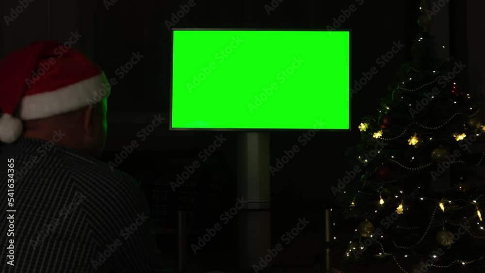 Man in Santa hat watching green screen TV mockup on black background ...