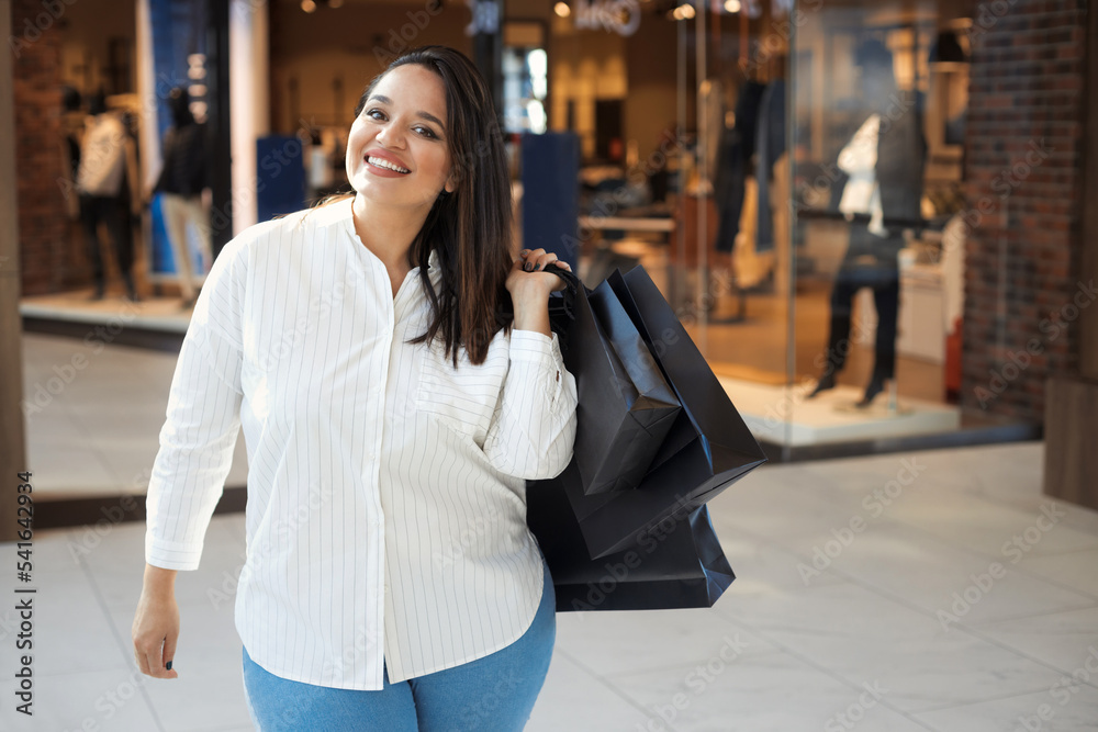Casual overweight woman in shopping mall with many purchases in paper ...