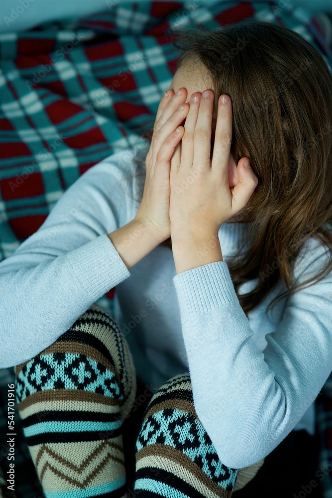 A teenage girl is sitting on the bed, an emotion of sadness and despair ...