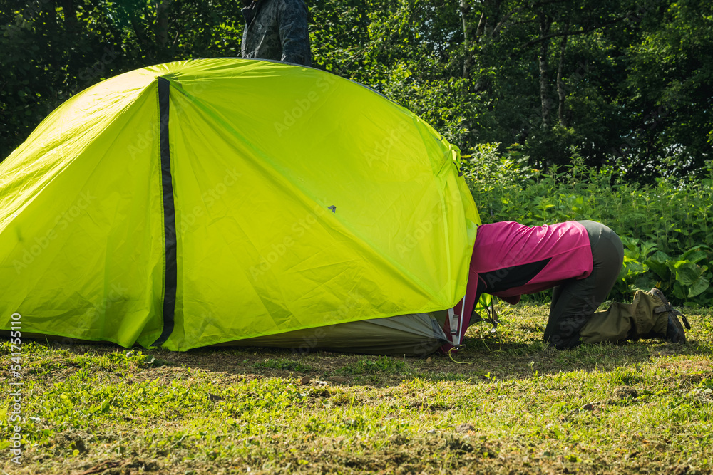 Fotka „Girl hiker in pants and purple jacket sets up tent while camping ...