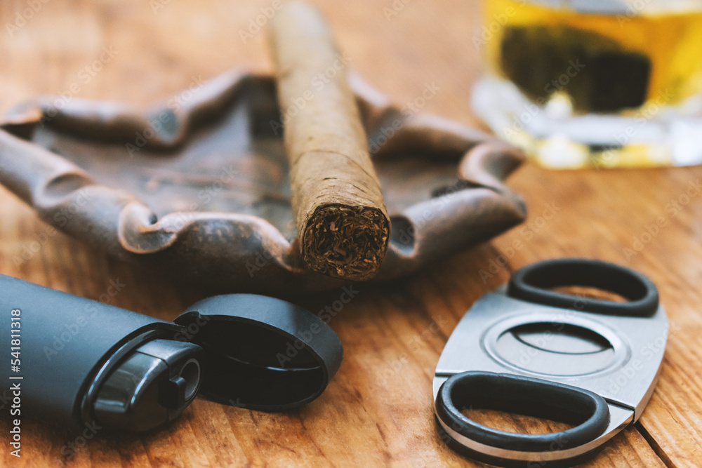 A cigar, a clay ashtray, a lighter and a guillotine lie on a wooden ...