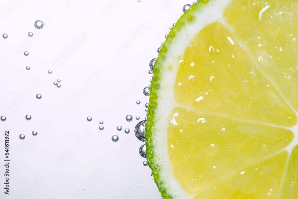Macro photo of lime slice In water with bubbles isolated on white background. Freshness and ...