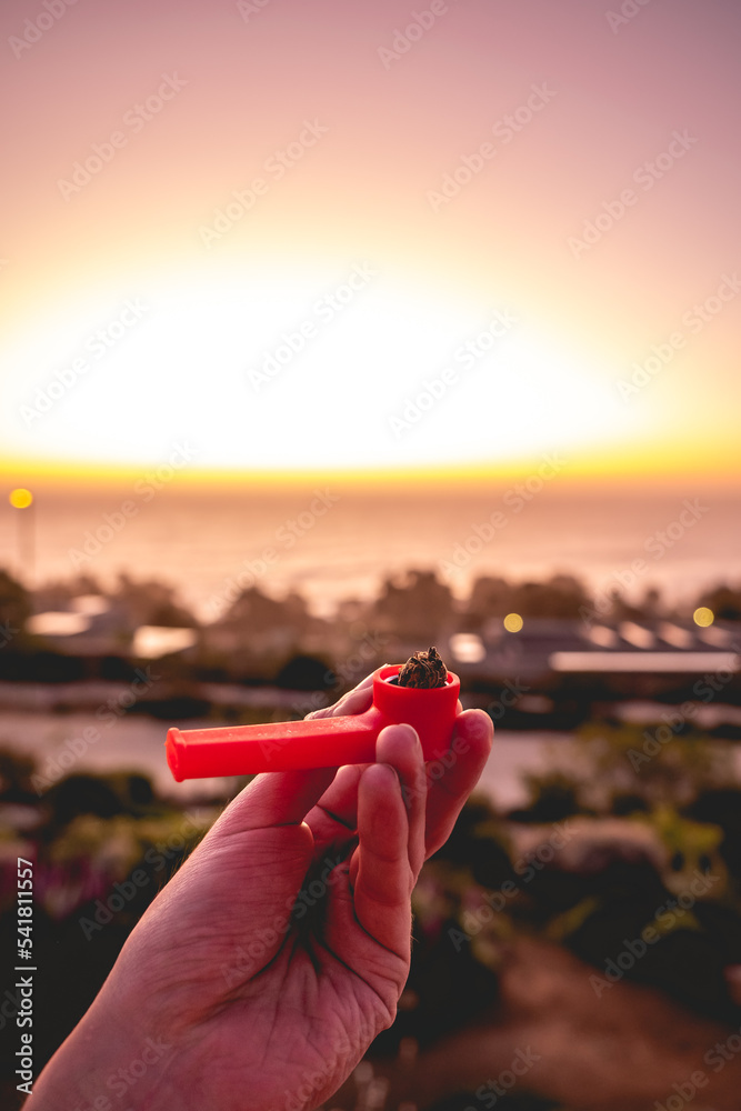 Hand holding a orange plastic marijuana pipe with weed with beautiful ...
