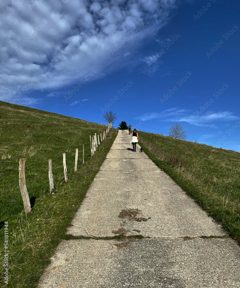 Wanderer gehen auf einem betonierten Weg neben einem Holzzaun vor ...