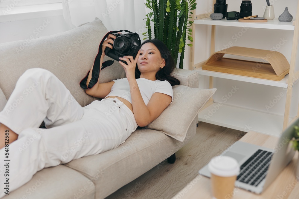 An Asian woman photographer lies on the couch with a camera and watches ...