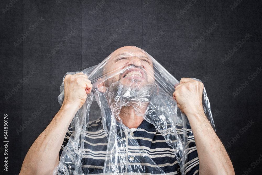 Mature man with a transparent plastic bag flying over his head and face ...