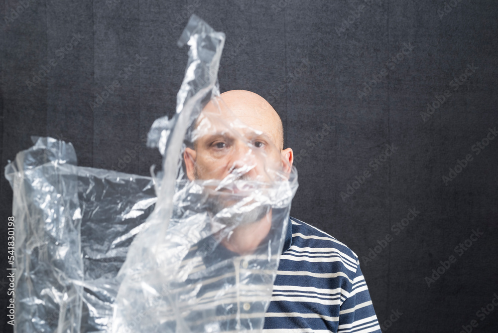 Mature man with a transparent plastic bag flying over his head and face ...
