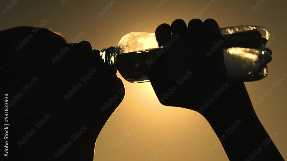 silhouette girl drinking water from bottle glare sun. man quenches ...