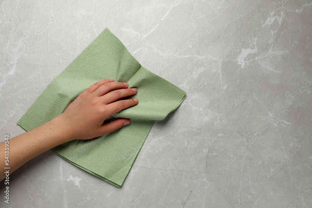 Woman cleaning light grey table with paper towel, top view. Space for ...