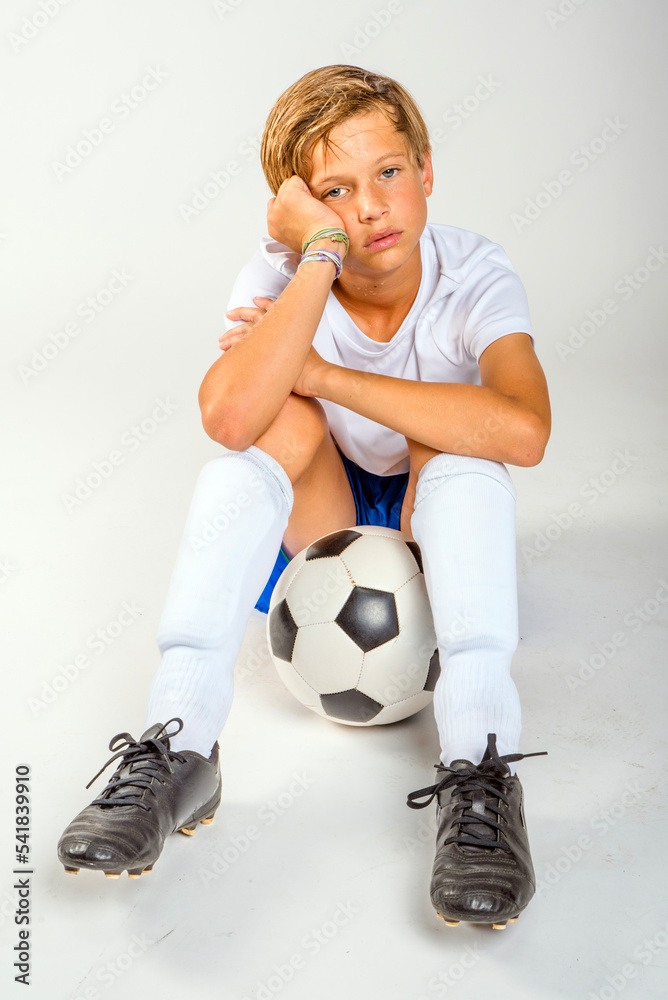 Exhausted soccer boy sadly sitting with his soccer ball after losing a ...