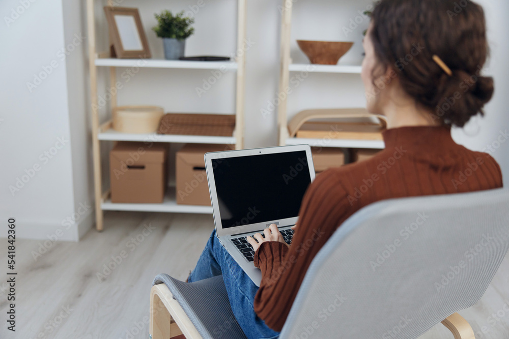 View from back of curly working woman sitting with laptop on knees in ...